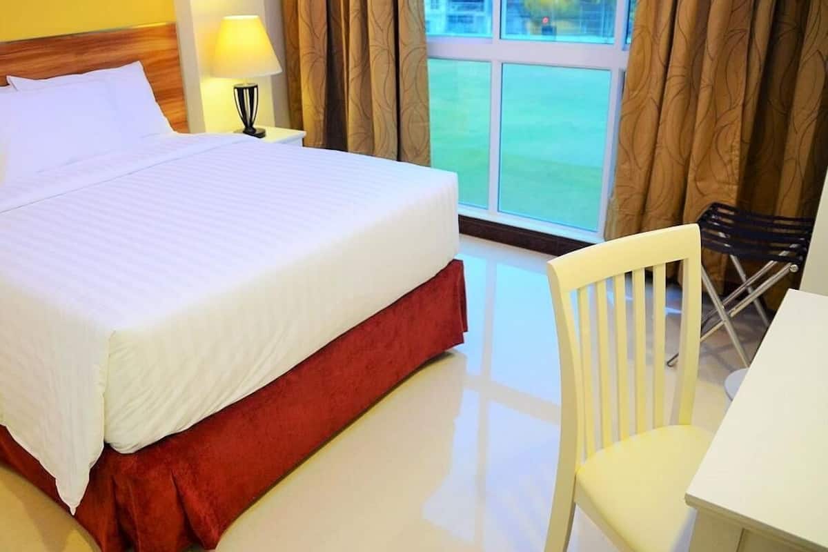 Quarto de hotel com cama, uma cadeira, uma mesa e janela com cortinas.