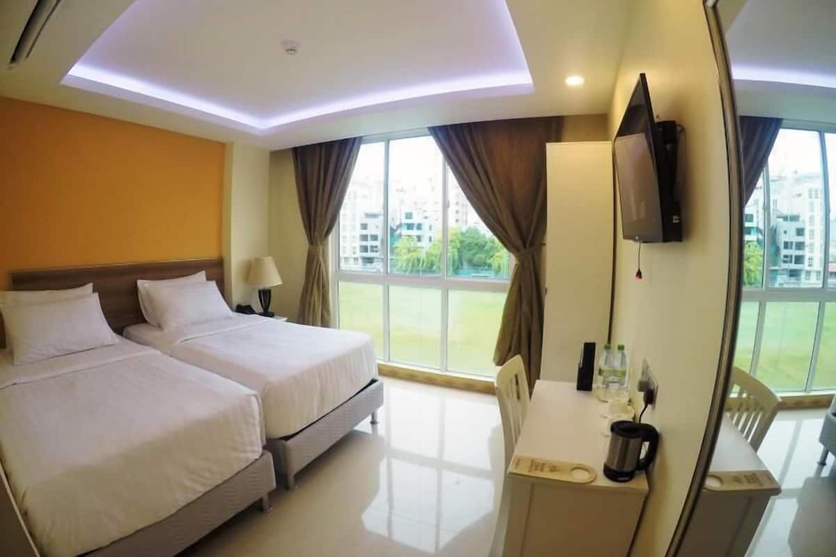 Quarto de hotel com duas camas, uma mesa de jantar, televisão e janelas amplas com cortinas.
