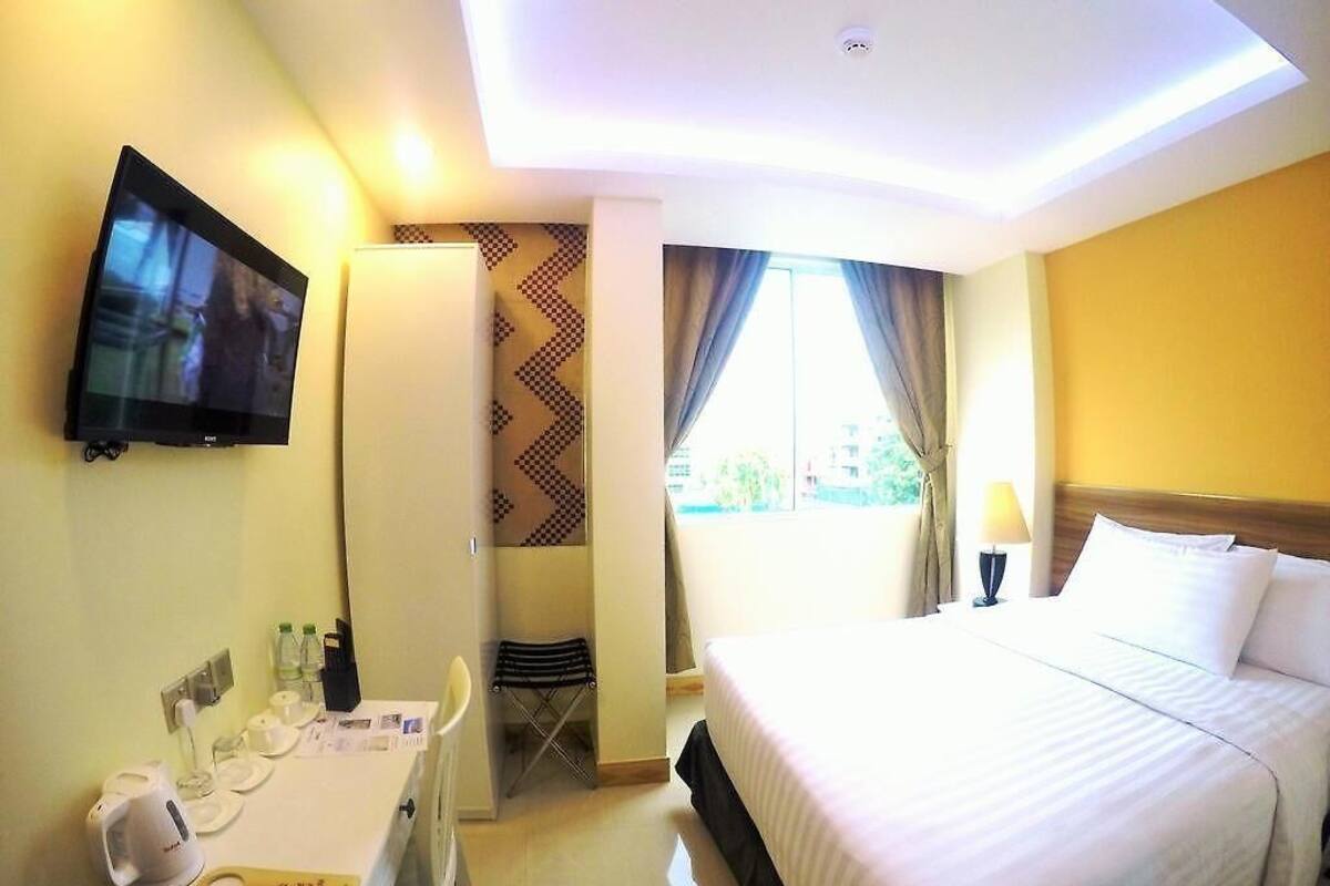Quarto de hotel com cama, escrivaninha com cadeira, televisão e janela com cortinas.