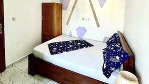 Um quarto com cama, mesa de cabeceira, abajur e guarda-roupa.
