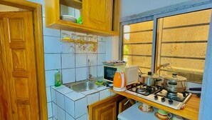 Uma cozinha compacta com armários de madeira, micro-ondas, fogão a gás e uma janela com persianas.