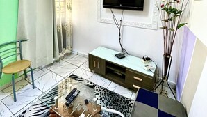Uma sala de estar com uma televisão de tela plana na parede, um sofá, uma mesa de centro e um vaso decorativo com flores.
