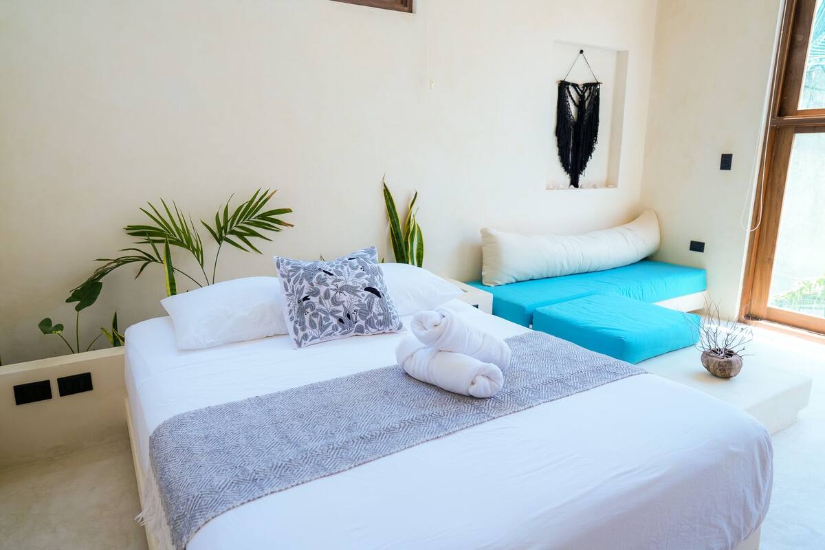 Quarto moderno com cama grande, um cantinho de estar e plantas em vasos.