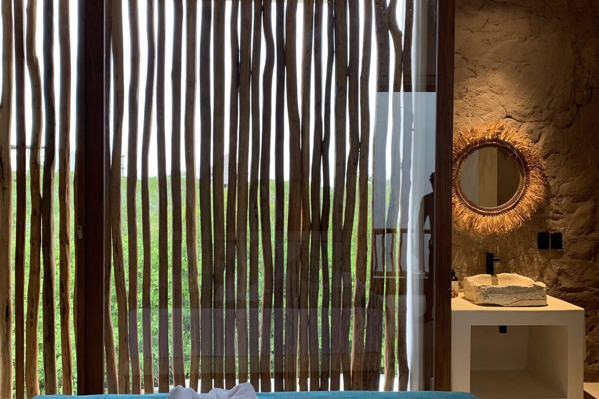 Quarto com uma cama, mesa de cabeceira, espelho e vista através de um separador de madeira.