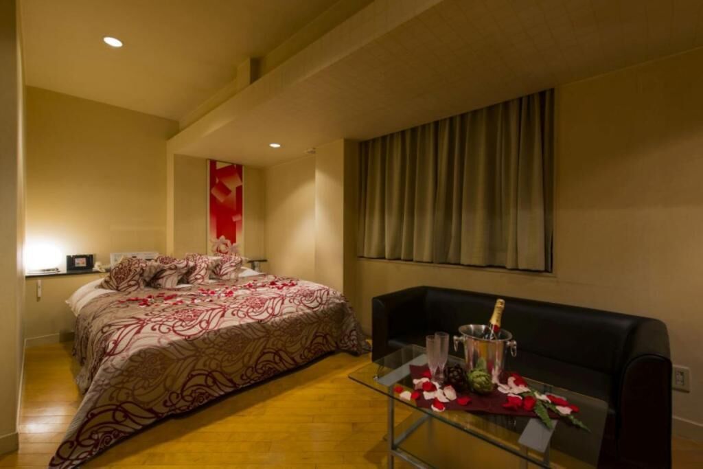 Um quarto com cama, uma mesa de centro de vidro com uma garrafa de champanhe, e um objeto decorativo vermelho na parede.