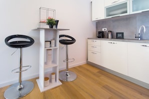 Uma cozinha moderna com armários brancos, uma pia de aço inoxidável e dois banquetas pretas.