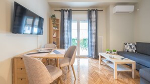 Uma sala de estar moderna com televisão de tela plana, um sofá, uma mesa de jantar com cadeiras e uma janela grande com cortinas.
