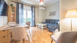 Uma sala de estar moderna com um sofá, cadeiras, uma mesa de centro, uma televisão e uma janela com cortinas.