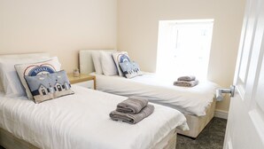 Quarto de hotel com duas camas de solteiro, cada uma com uma almofada e uma toalha dobrada.