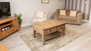 Uma sala de estar com uma mesa de centro de madeira, uma TV sobre um suporte de madeira, uma parede listrada, um sofá e um quadro na parede.