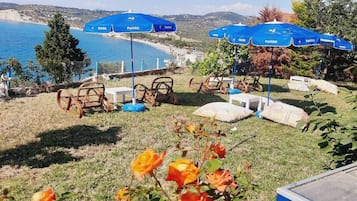 Um terraço com área de estar ao ar livre, guarda-sóis azuis e vista para o mar.