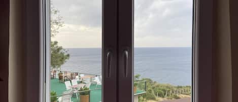 Vista pela janela com uma varanda sobre um corpo de água, com cadeiras e mesas dispostas na varanda.