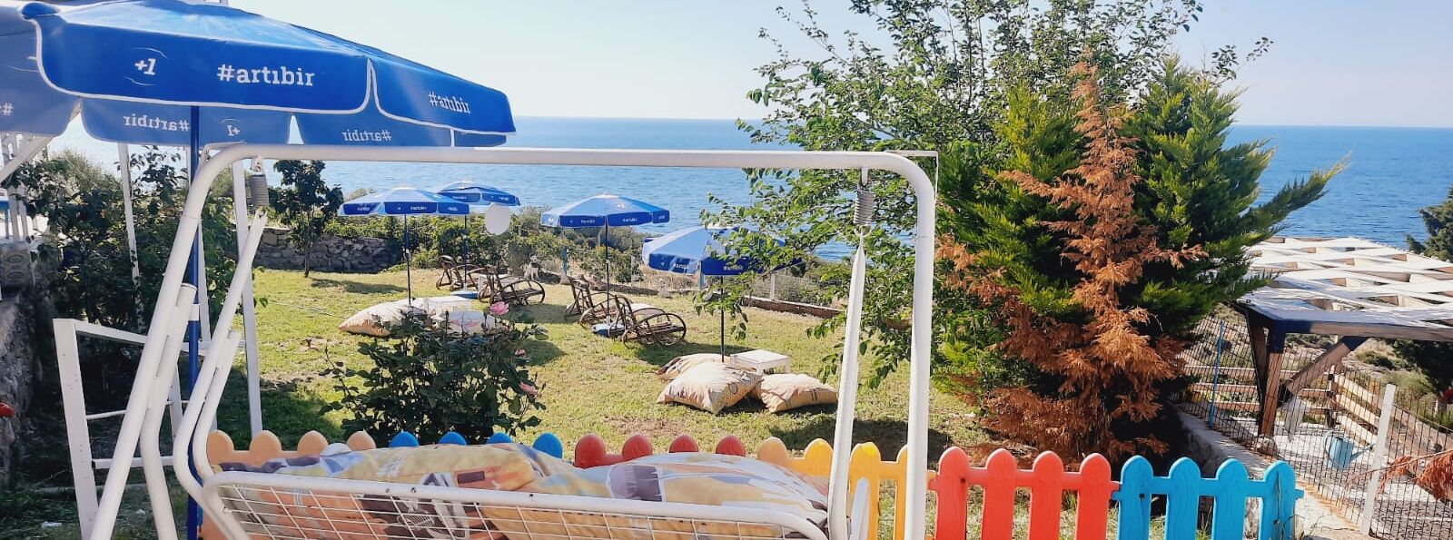 Vista de uma área à beira-mar com guarda-sóis, assentos e um jardim cercado.