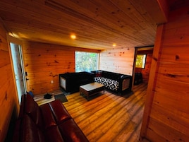 Interior de uma cabana de madeira com sofá, televisão e um banco.