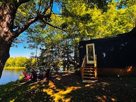 Uma cabana à beira de um lago, com um píer, rodeada por árvores.