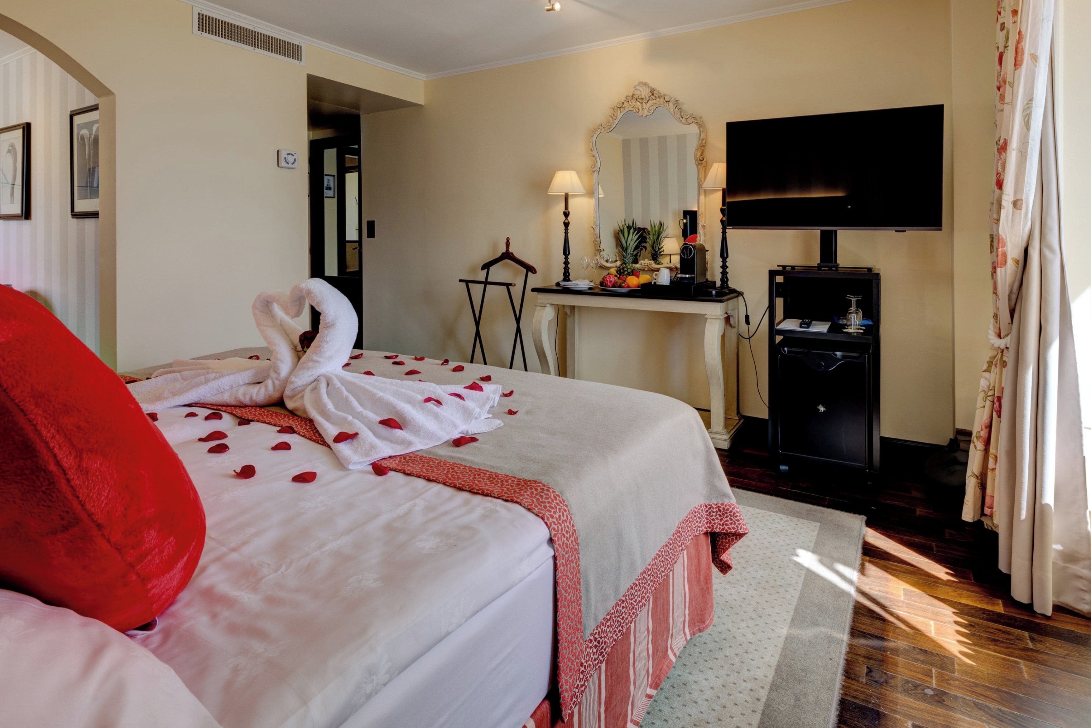 Quarto de hotel com uma cama, escrivaninha com espelho, televisão e guarda-roupa.