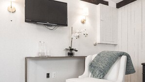 Uma sala de estar moderna com um sofá branco, uma TV de tela plana fixada na parede, uma pequena mesa de console com objetos decorativos e um tapete estampado.