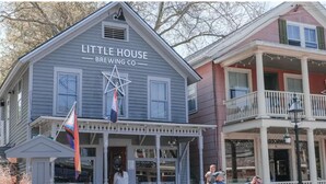Um edifício com a placa 'Little House Brewing Co.', área de estar ao ar livre e varanda.