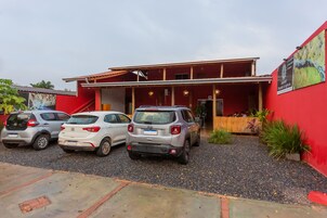 Um edifício com fachada vermelha, entrada coberta e três carros estacionados em frente.