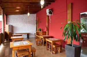 Interior de restaurante com mesas e bancos de madeira, parede de pedra e uma grande planta em vaso.