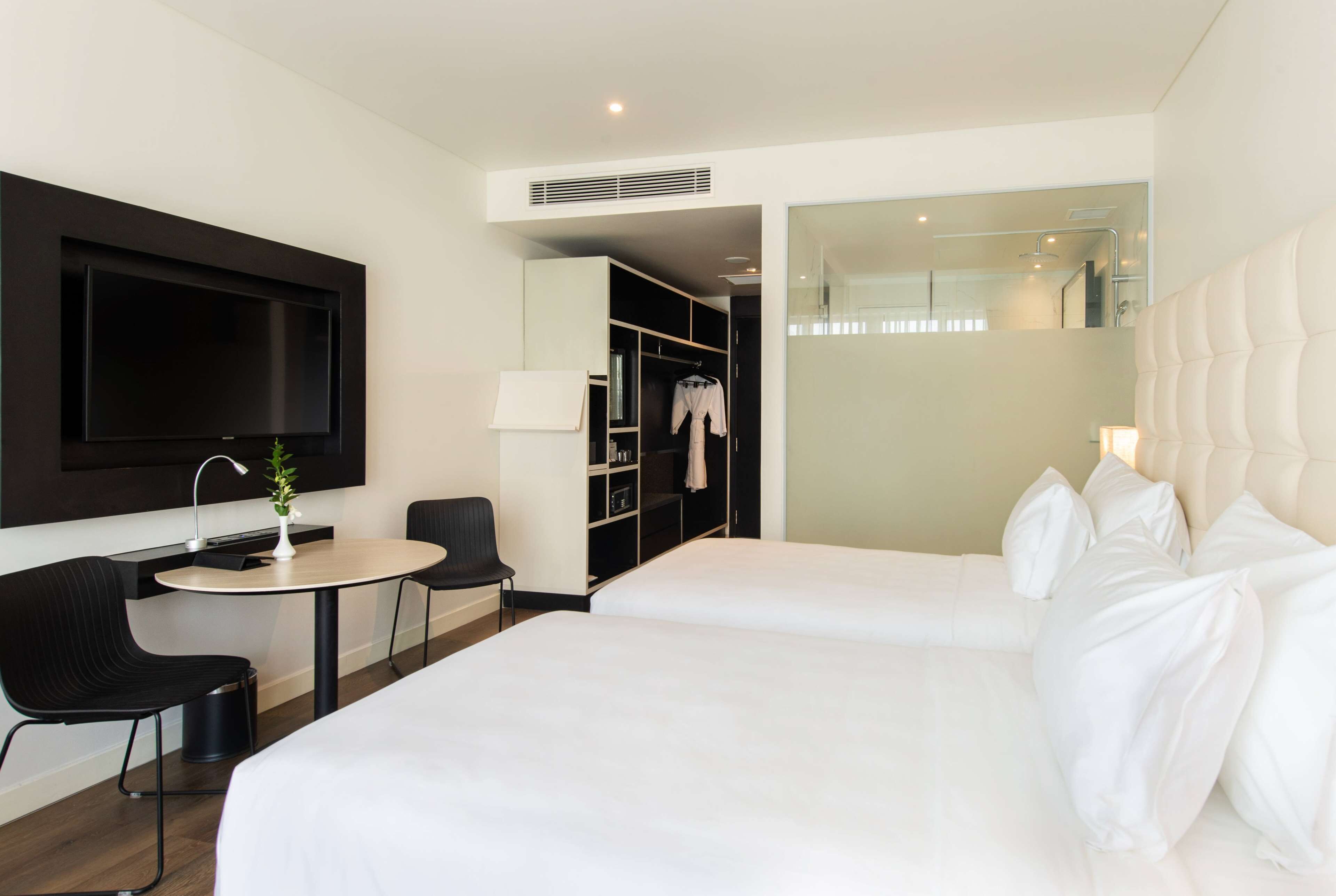 Quarto de hotel com uma cama grande, uma escrivaninha com cadeira, televisão na parede e um closet espaçoso.