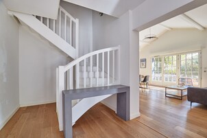 Interior moderno com escada de madeira, mesa consola cinzenta e sala de estar com sofá e mesa de centro.