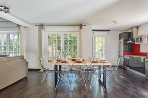 Cozinha moderna com área de jantar, apresentando uma mesa de madeira, cadeiras transparentes e bancada vermelha.