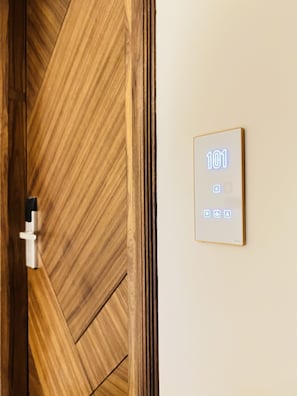 Uma porta de madeira com fechadura moderna e um painel de controle fixado na parede exibindo o número 101.