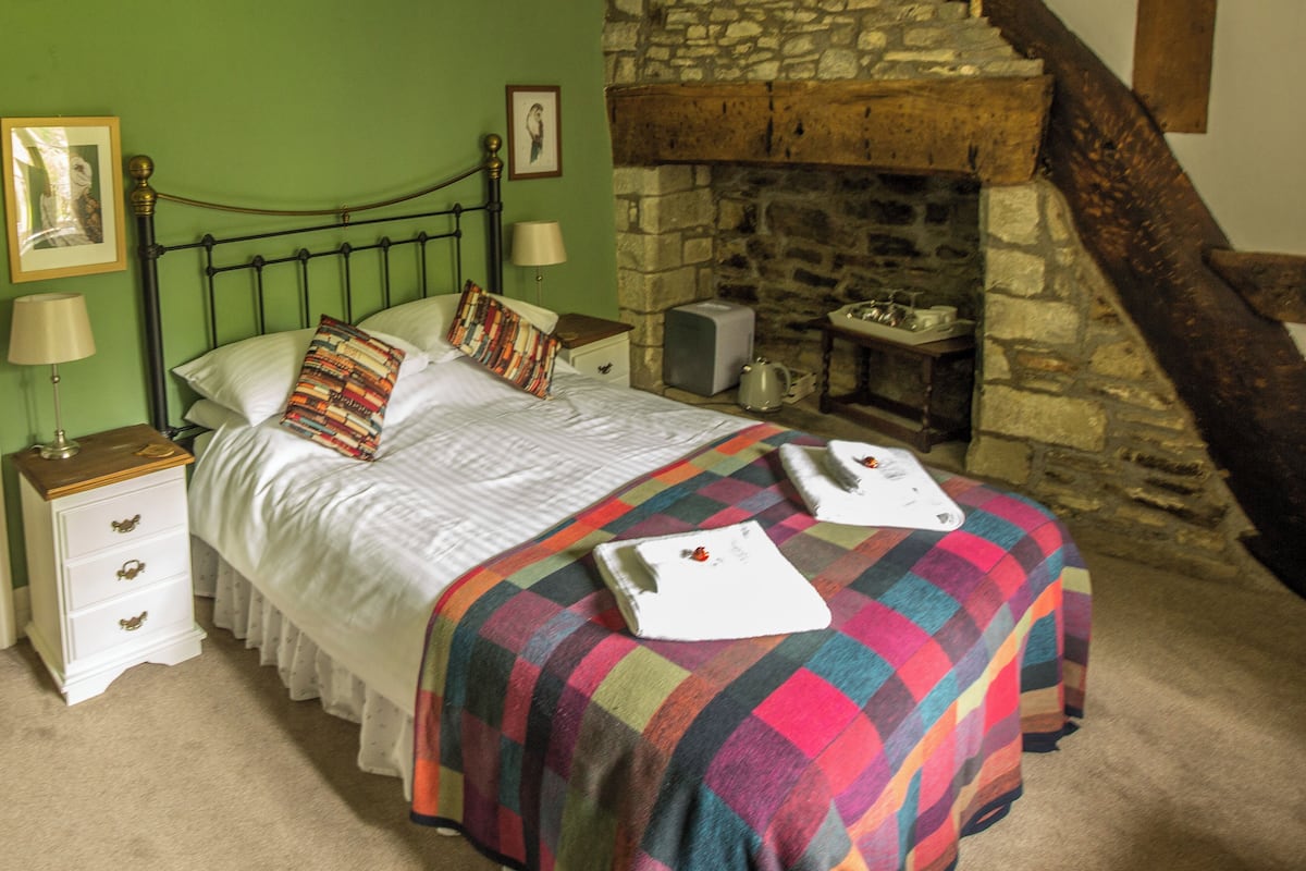Um quarto com cama, mesa de cabeceira, abajur, lareira de pedra e escada de madeira.