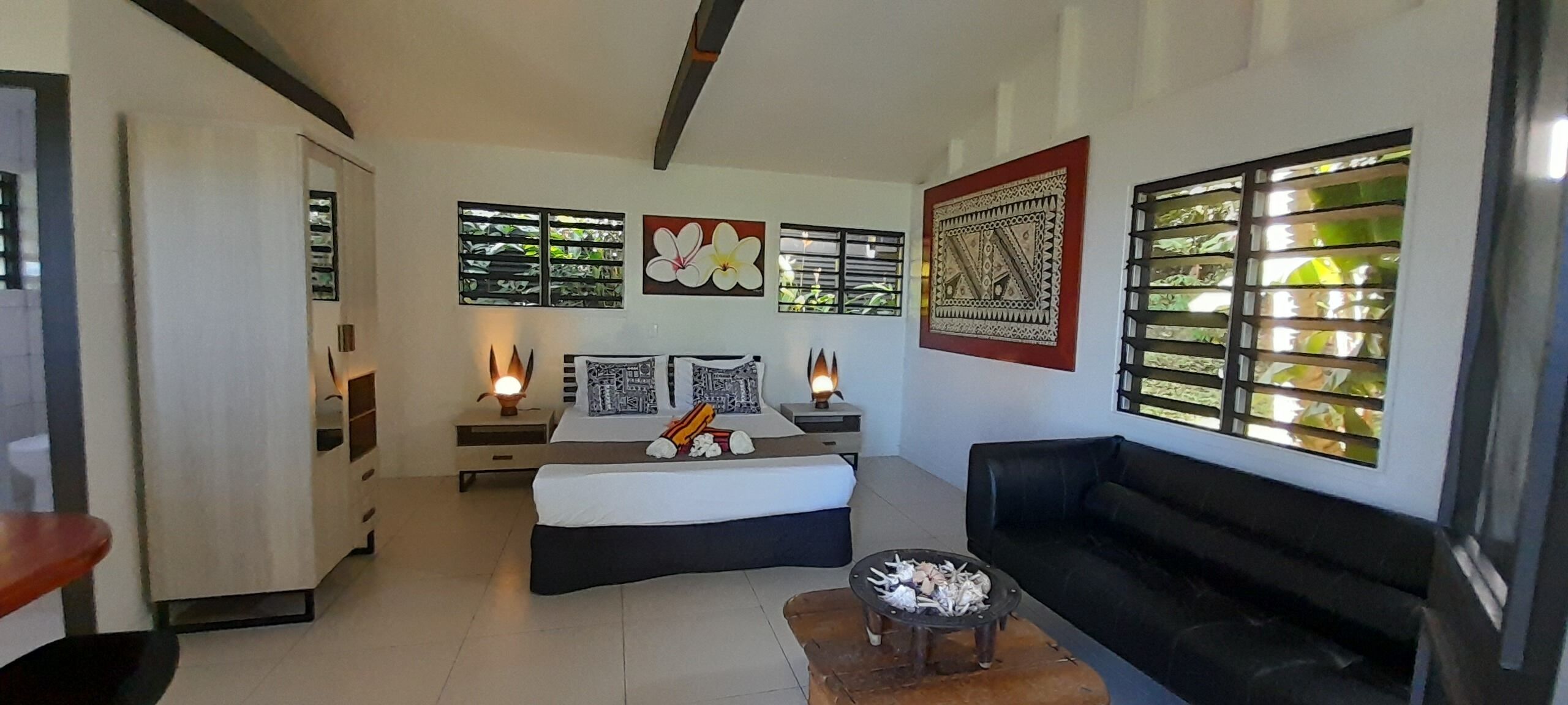Um quarto com cama, mesas de cabeceira, um sofá preto e uma pequena mesa com objetos decorativos.
