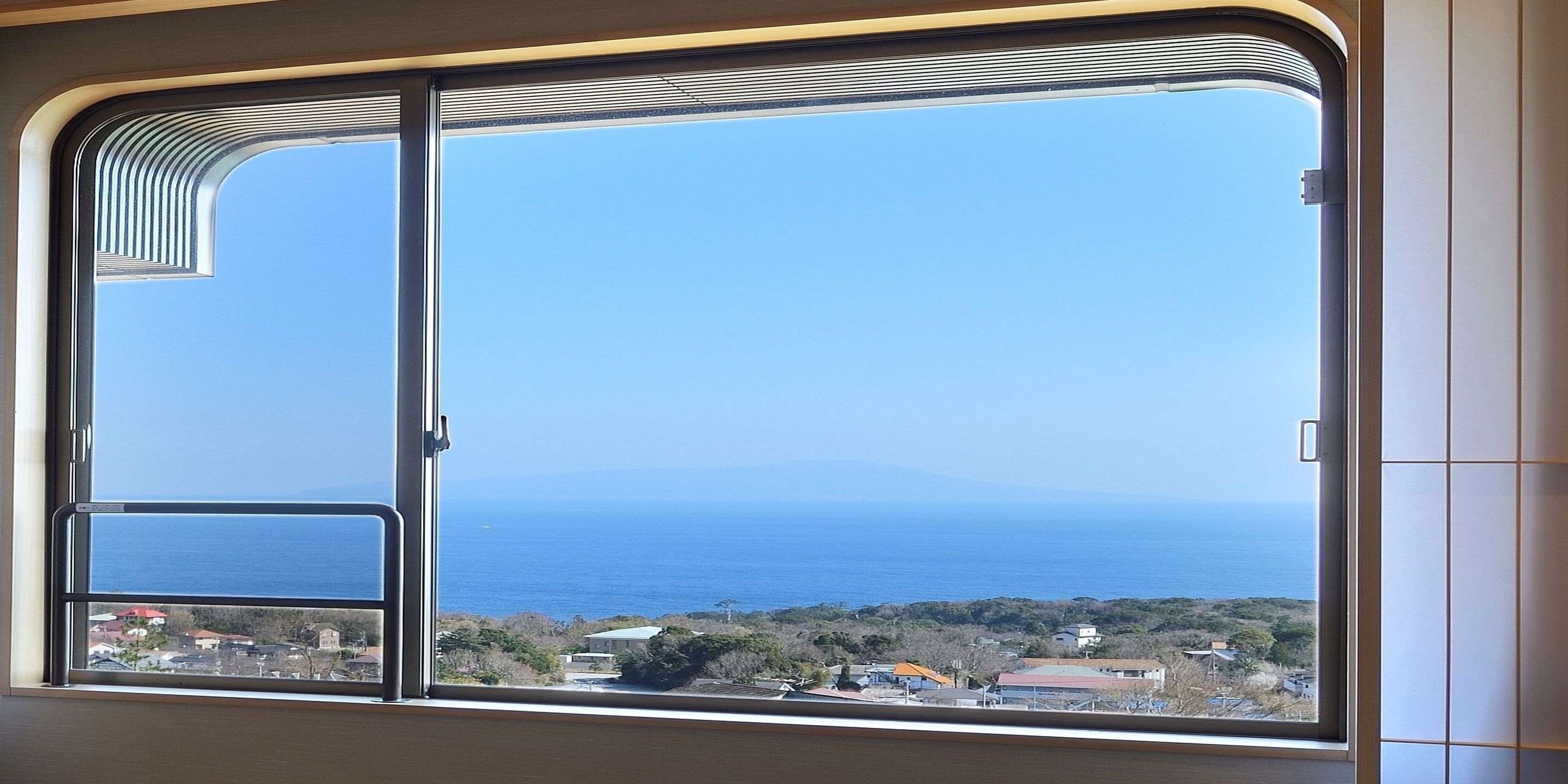 Um quarto com uma janela grande que oferece vista para o mar e edifícios ao longe.