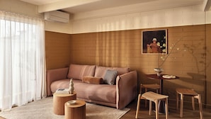Uma sala de estar aconchegante com parede de tijolos marrons, um sofá castanho, uma mesa de madeira pequena e um banquinho de madeira redondo.