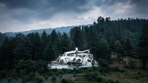 Um edifício moderno, com vários níveis e um design arquitetônico único, rodeado por uma floresta densa e montanhas.