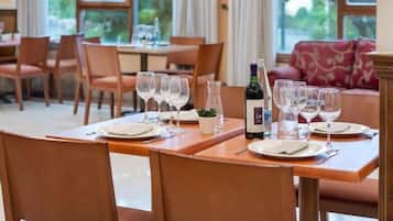Uma área de refeições com mesas e cadeiras de madeira, copos de vinho e uma garrafa de vinho.