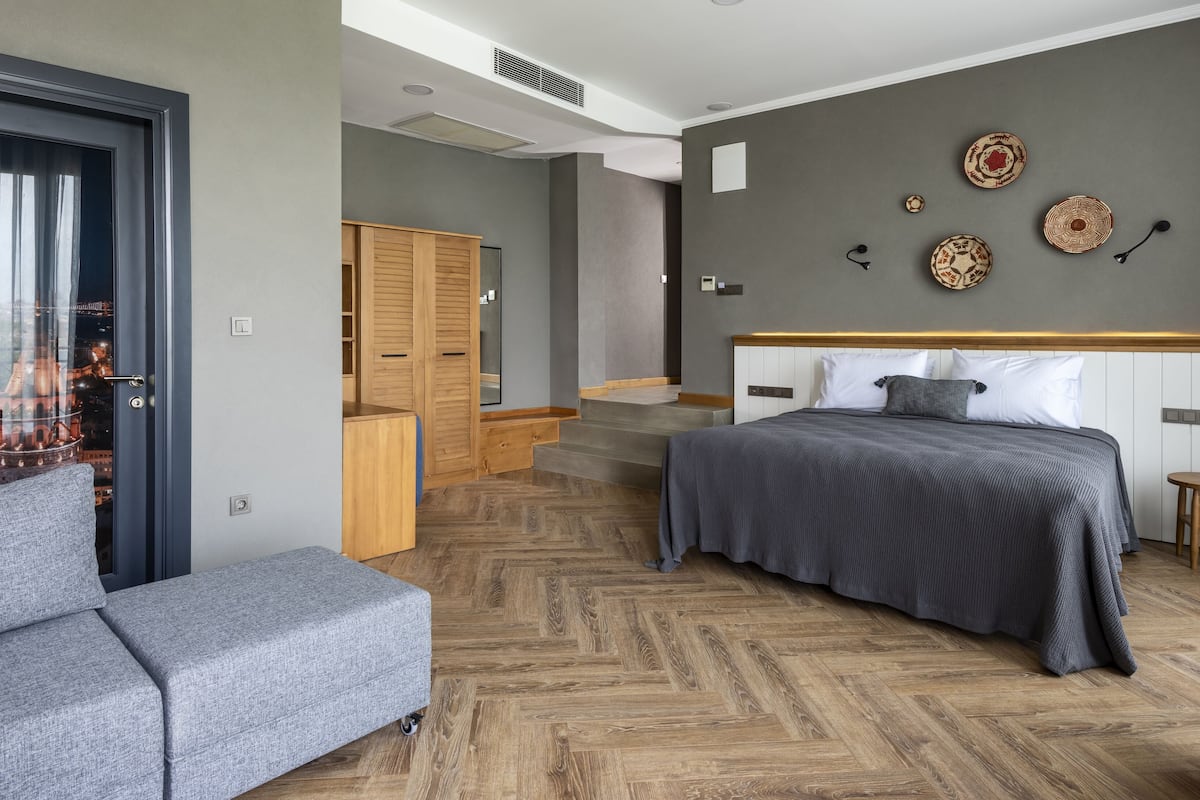 Quarto de hotel moderno com cama, sofá, guarda-roupa de madeira e escada.