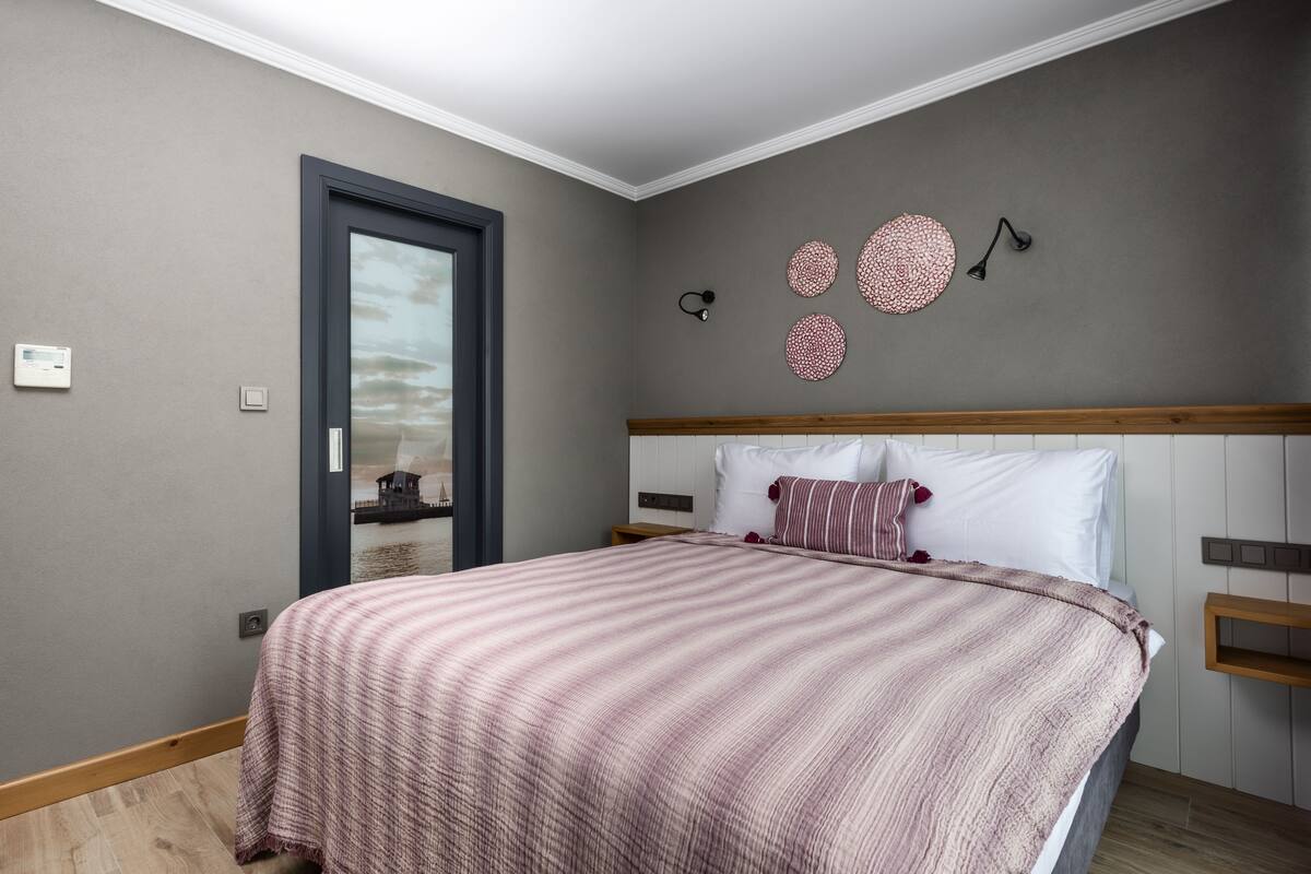 Quarto com cama, cabeceira de madeira, mesa de cabeceira e luminária na parede.