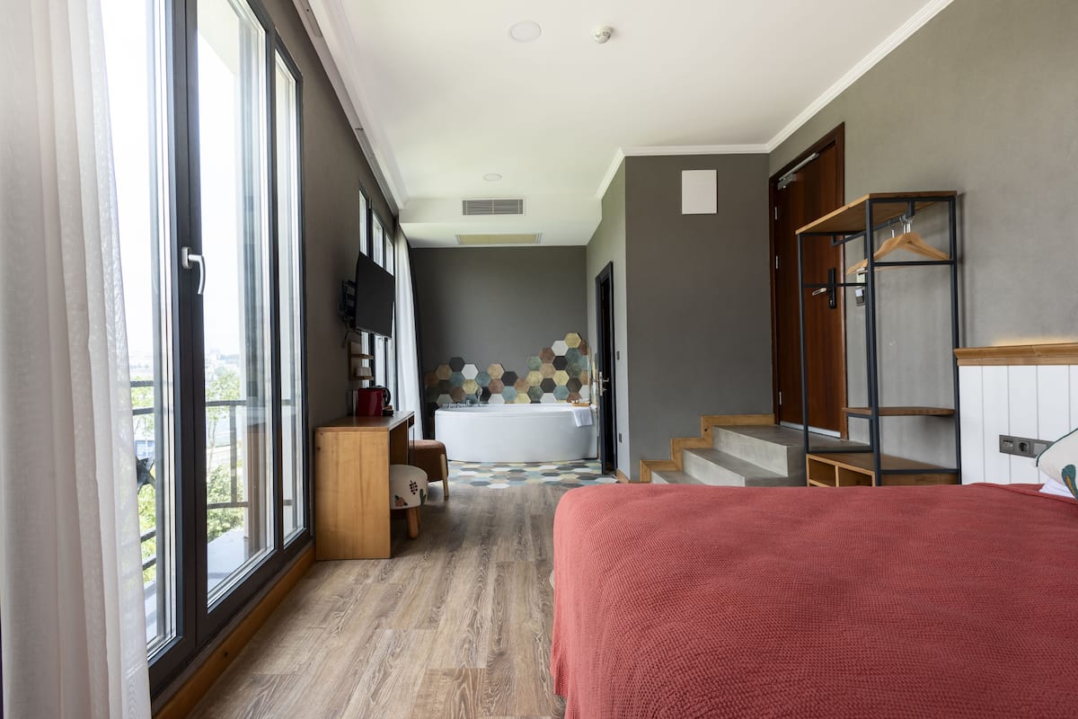 Quarto moderno com uma cama grande, uma escrivaninha, uma cadeira, uma banheira e um guarda-roupa.