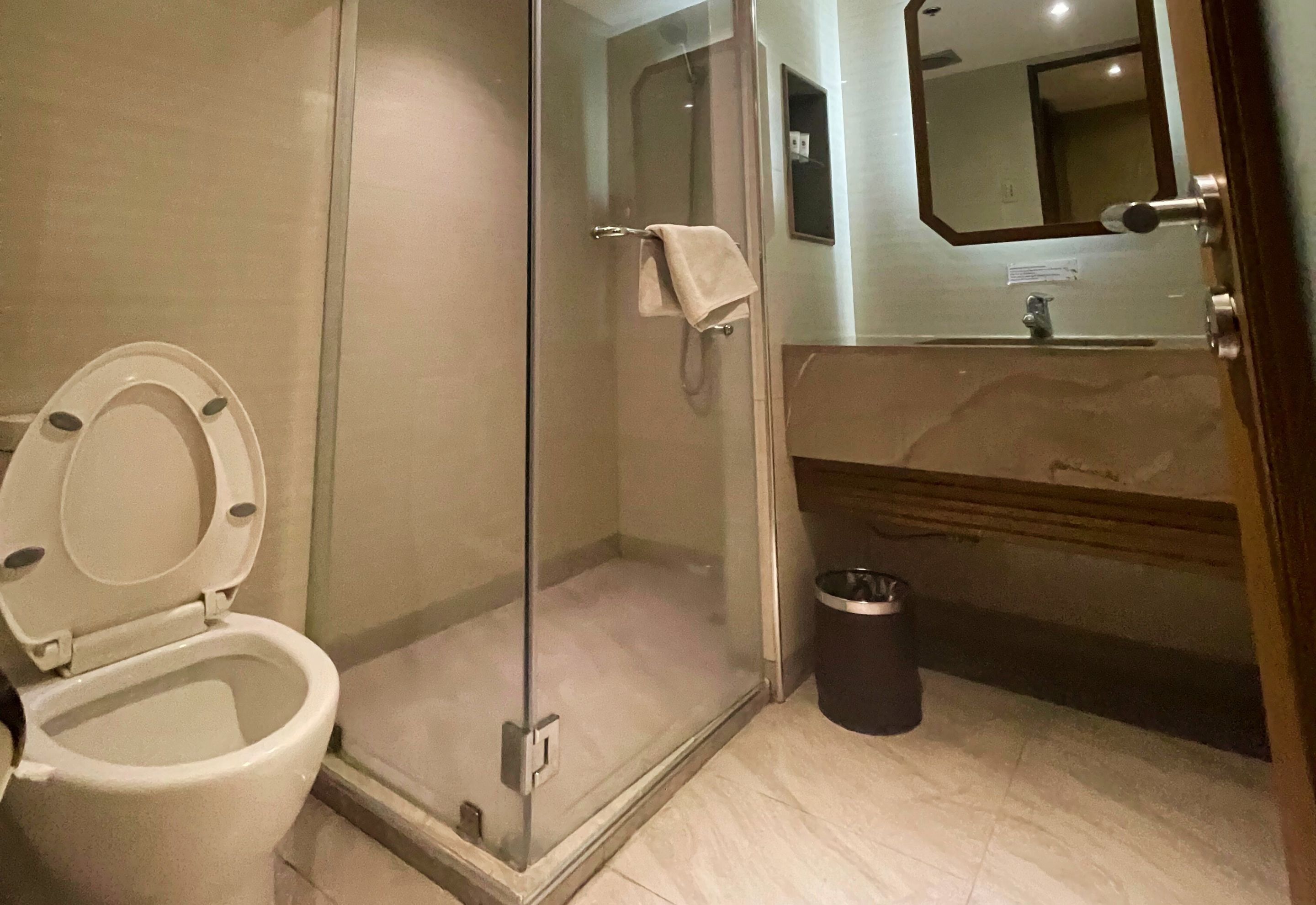 Um banheiro com vaso sanitário, chuveiro com box de vidro, pia e lixeira.