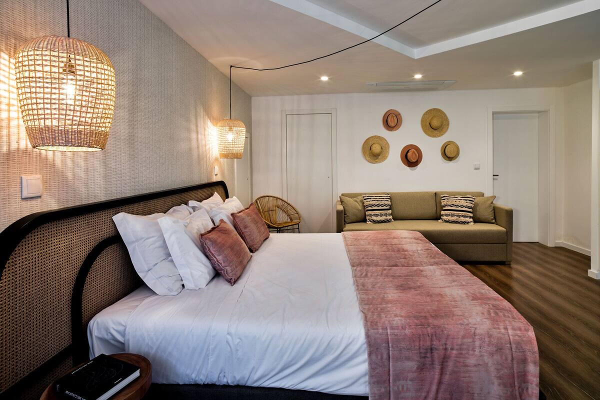Quarto moderno com cama grande, um sofá e chapéus decorativos na parede.