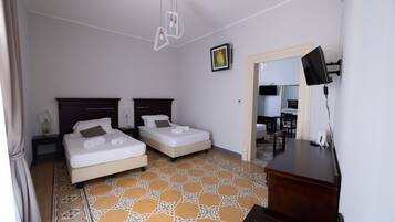 Quarto de hotel com duas camas, uma escrivaninha, uma cadeira, uma televisão e um chão com padrão.
