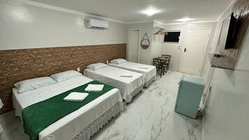 Quarto de hotel com duas camas, uma mesa pequena, uma cadeira, TV e geladeira.