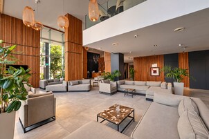 Um hall espaçoso com uma ampla área de estar, balcão de recepção e design moderno com detalhes em madeira e grandes janelas.
