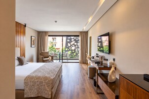 Quarto de hotel com cama, escrivaninha, cadeira e vista pela janela.