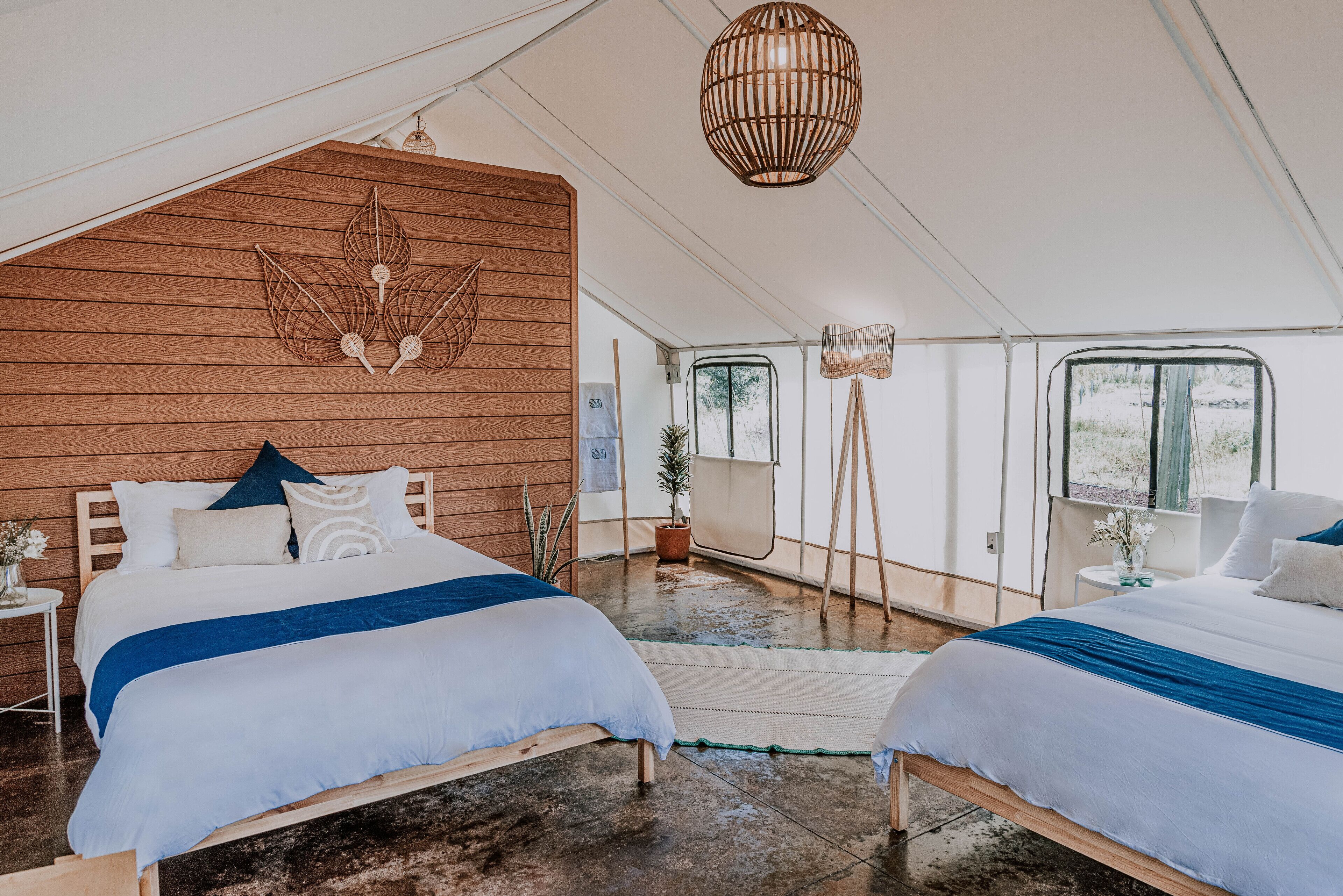 Quarto tipo tenda com duas camas, paredes de painel de madeira e uma janela grande.