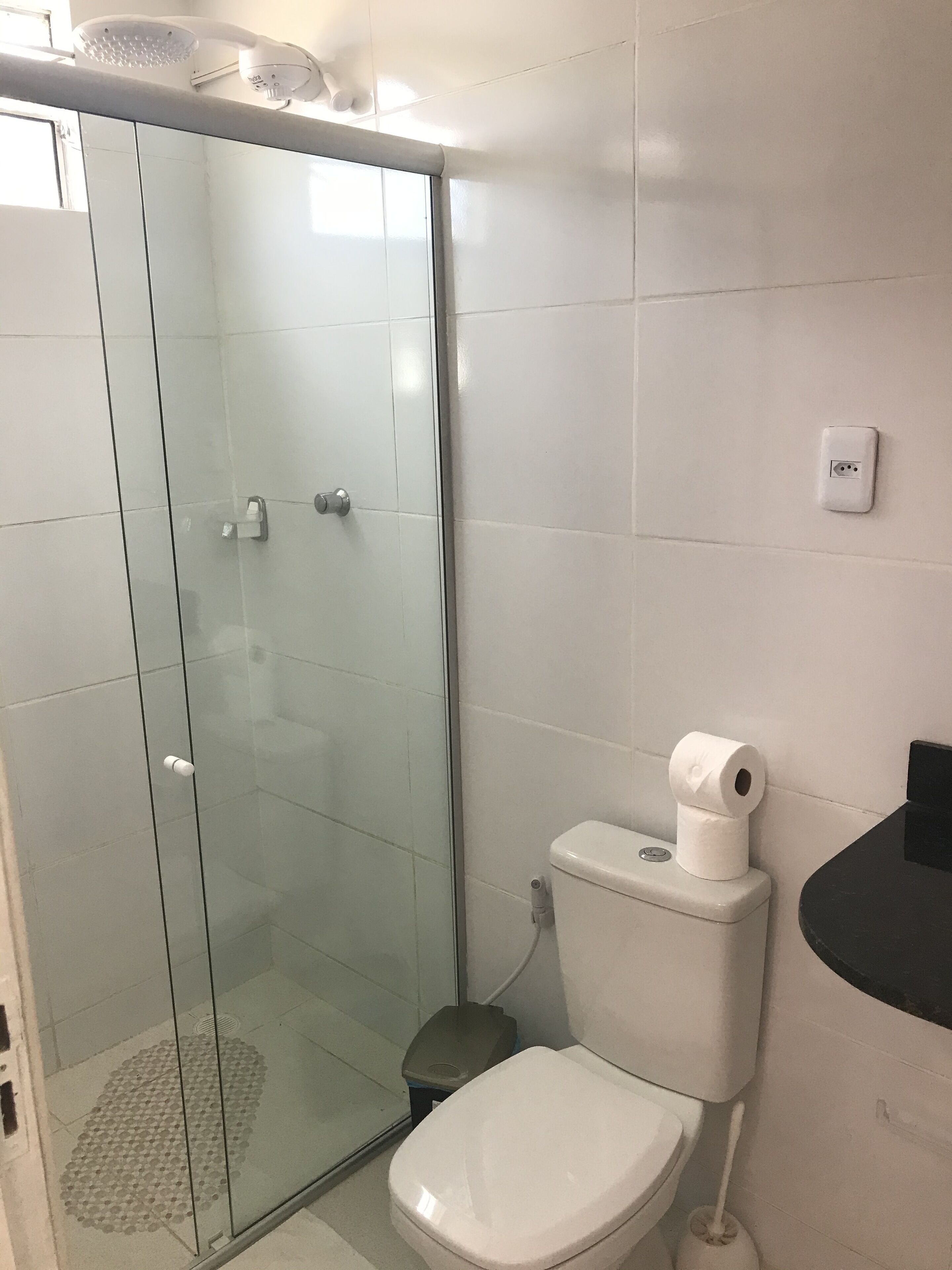 Casa de banho com cabine de duche em vidro, sanita e bancada preta.