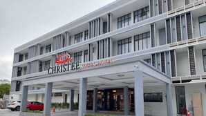 Um hotel moderno com entrada coberta, vários andares e um logotipo em destaque.