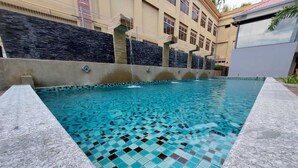 Uma piscina com piso azulejado e parede de pedra ao fundo.