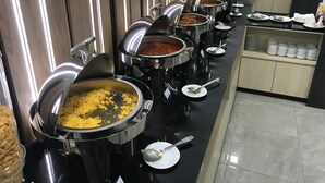 Montagem de buffet com várias estações de comida, cada uma com uma panela tampada e uma colher.