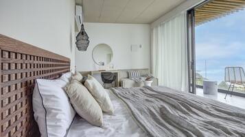 Quarto moderno com uma cama grande, cabeceira de madeira, espelho redondo, mesinha e vista para o exterior.