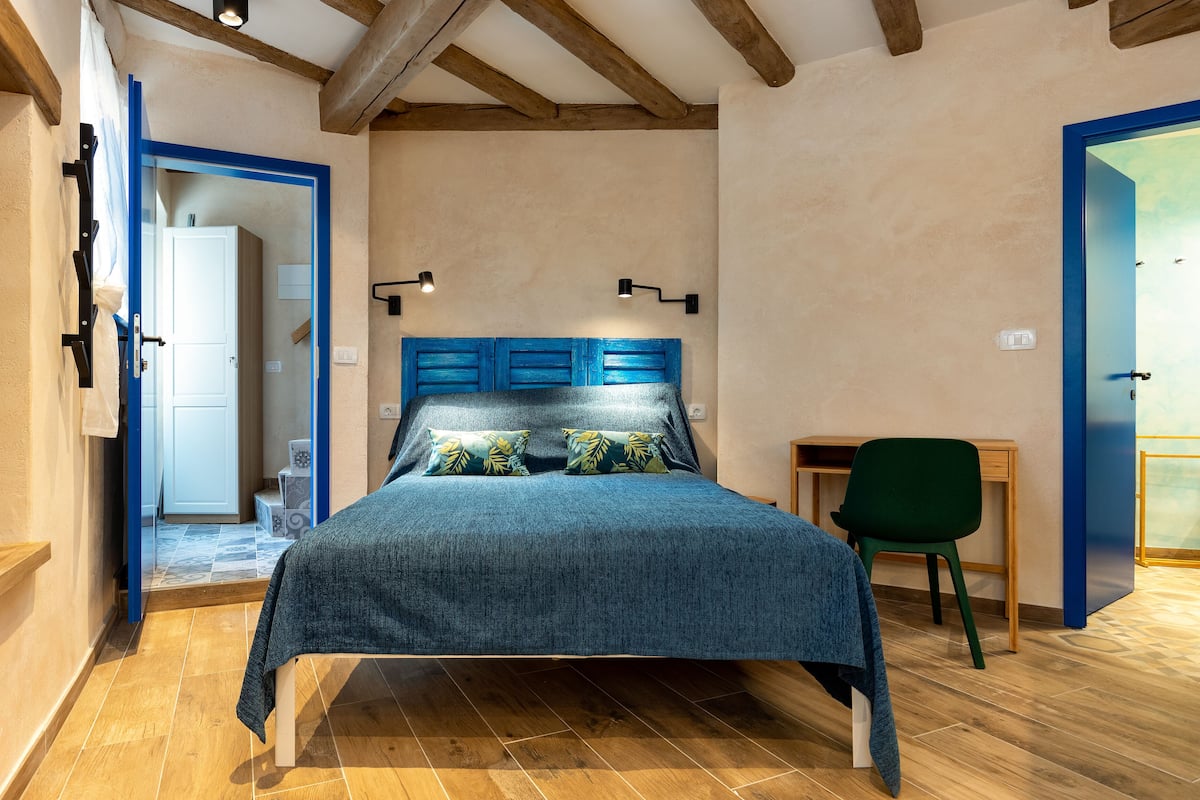 Quarto com cama, piso de madeira e escrivaninha com cadeira.